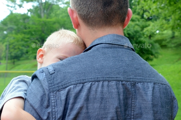 A little boy peeking over the shoulder of the man who is holding him ...