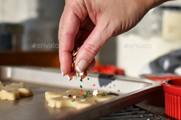 Sprinkling red, green and white sprinkles onto Christmas cutout cookies ...