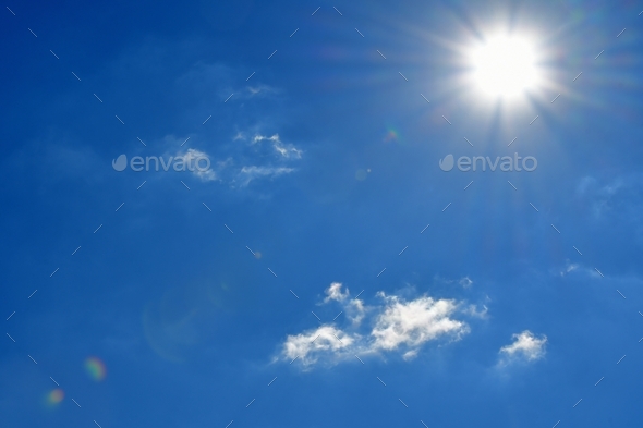 vivid blue sky with the sun shining giving off sunbursts and sun flares with a few wispy clouds ...
