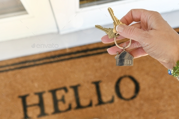 Female hand holding a set of keys over a welcome mat that says HELLO ...