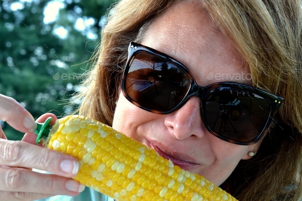 Woman eating corn on the cob, smiling after taking a bite of corn Stock ...