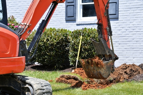 Backhoe digging dirt in lawn to install electrical & gas lines. Digging ...