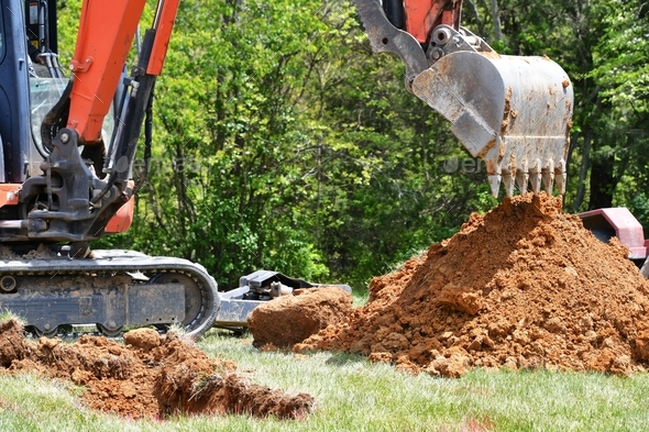 Backhoe digging dirt in a lawn to install electrical & gas lines ...