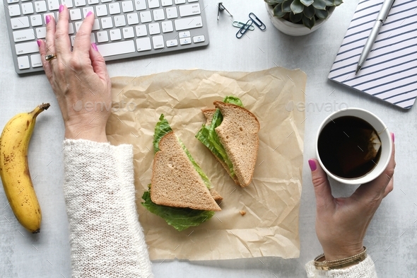 Female eating sandwich banana at desk - working through lunch hour ...