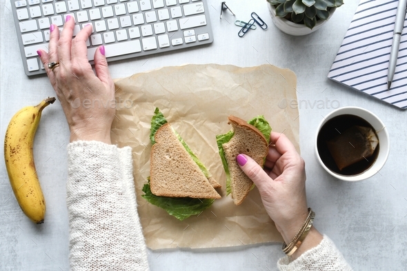 Female eating sandwich banana at desk - working through lunch hour ...