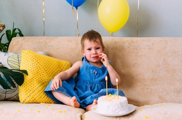 A little cute girl is celebrating her birthday at home, upset, crying ...