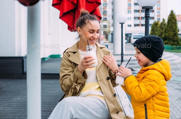Young mom and son have fun and drink milkshake outdoors. Family time ...