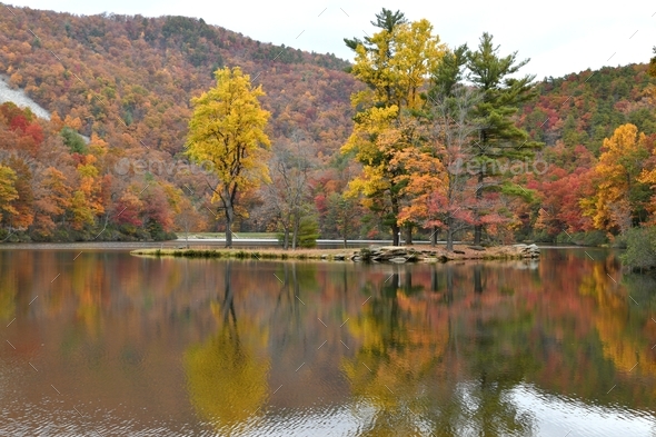 Trees on an island with colorful fall foliage reflecting in a mountain ...
