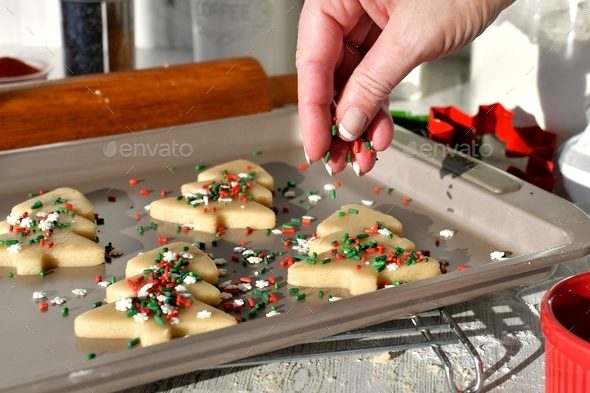 Sprinkling red, green and white sprinkles onto Christmas cutout cookies ...