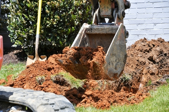 Backhoe digging dirt in lawn to install electrical & gas lines. Digging ...