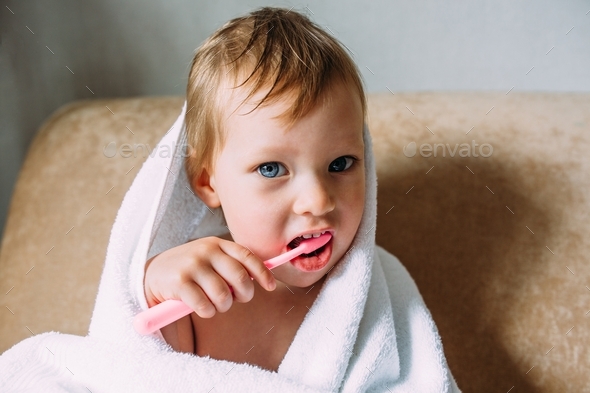 Cute child in big white towel. She brushes his teeth with toothbrush on ...