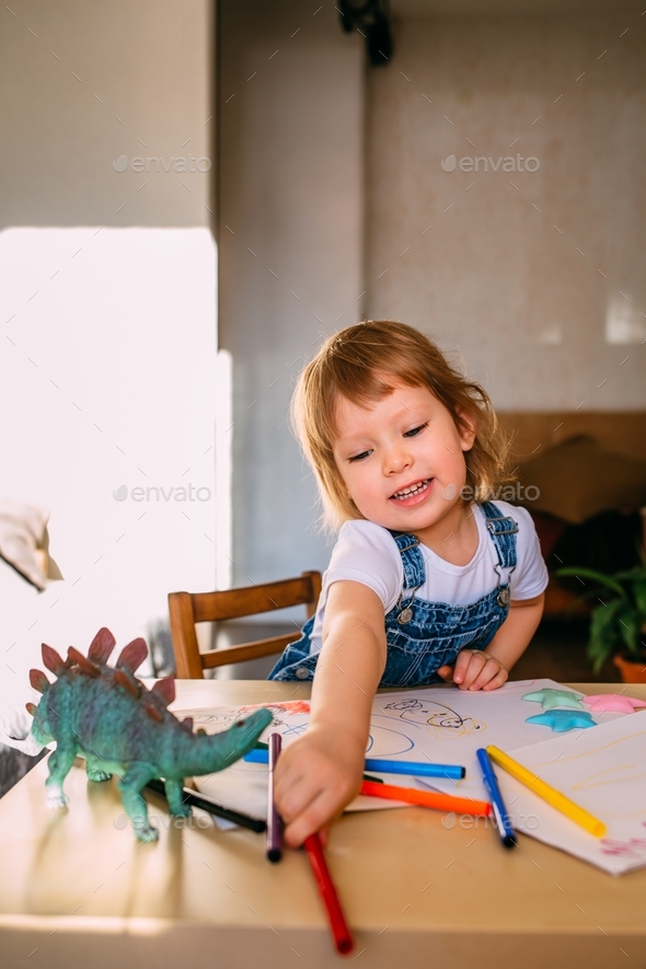 A small child at home at the children's table draws with felt-tip pens ...