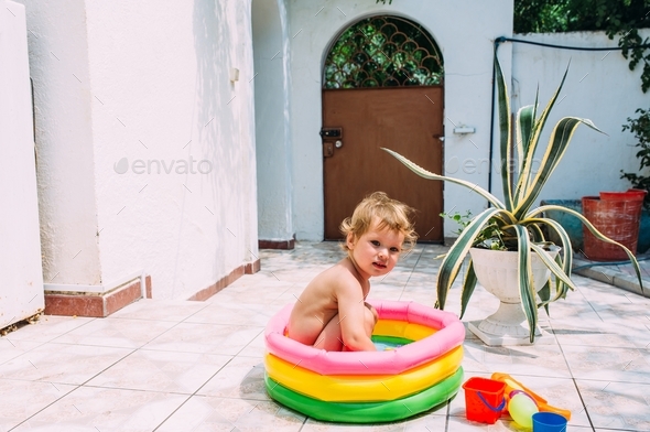 A cute child has fun and rejoices in an inflatable pool with toys in ...