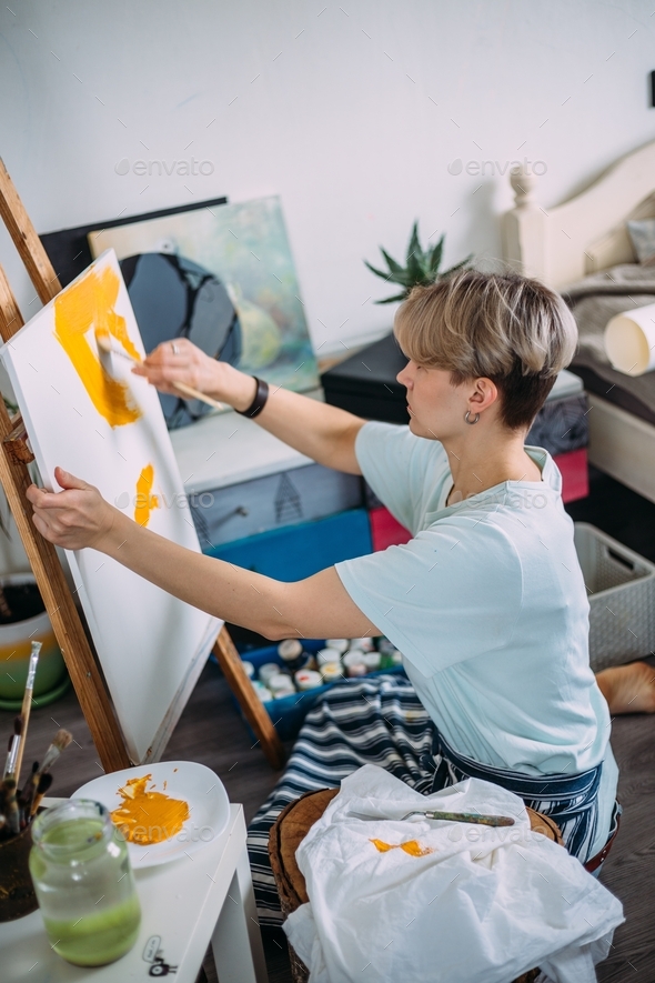 Young woman artist is painting at home in a creative studio setting ...