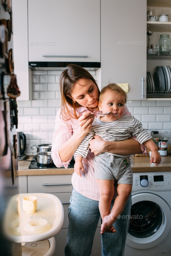 Mom feeds a small child at home with yogurt from a spoon. Family ...