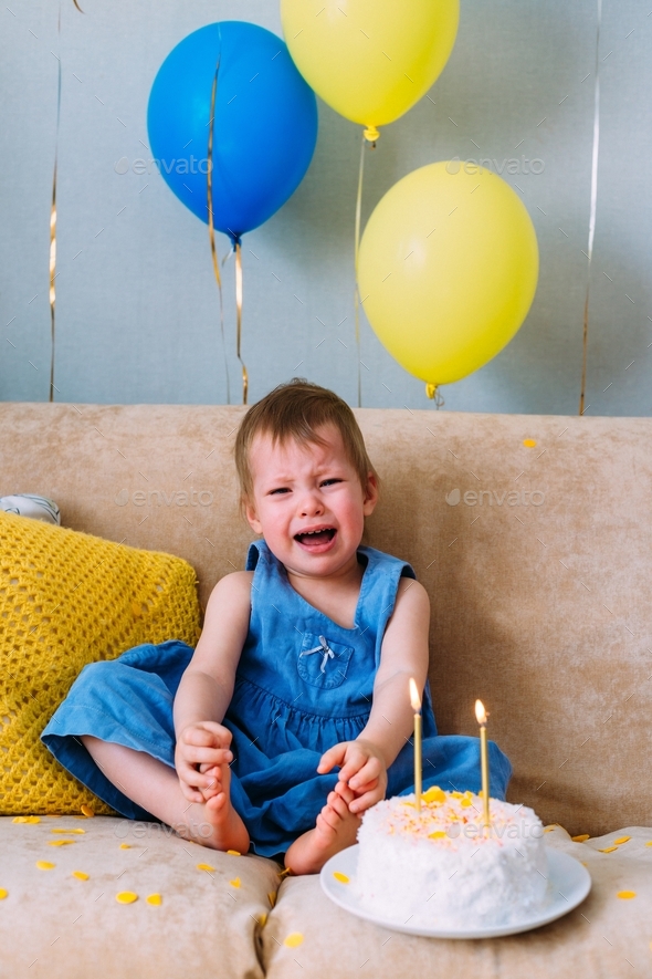 A little cute girl is celebrating her birthday at home, upset, crying ...