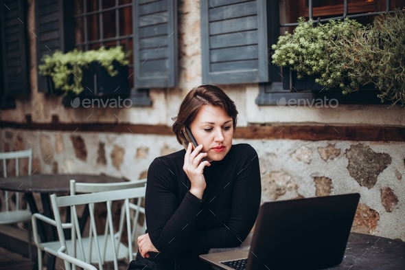 Beautiful busy woman working remotely with laptop and talking by ...