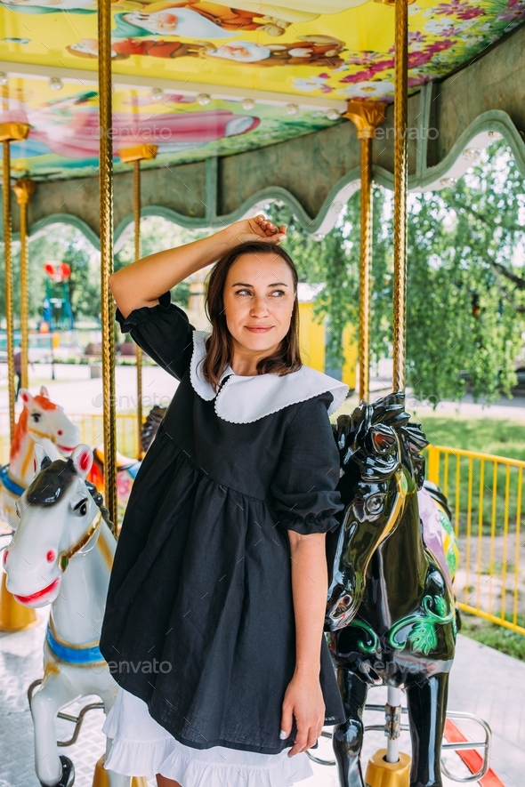Woman in dress poses on a bright carousel with horses in summer day ...