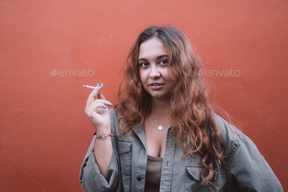 Pretty curly haired woman smoking by coral wall, bad habit Stock Photo ...