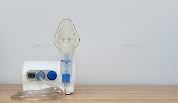The nebulizer for inhalation stands on a table against a gray wall ...