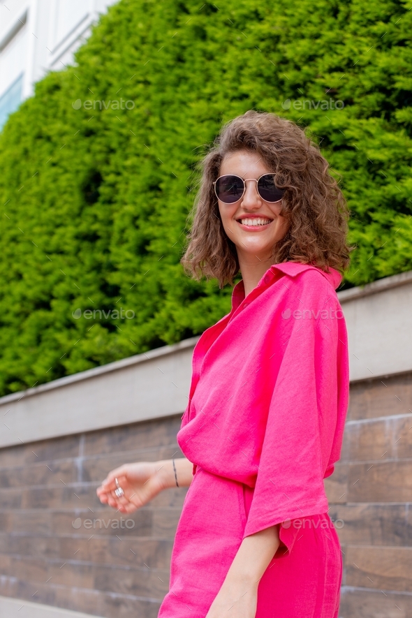 Candid portrait of beautiful young woman in bright pink shirt on nature ...