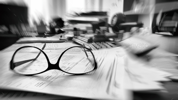 Routine day at the office, messy desk with lot of papers. Black and ...