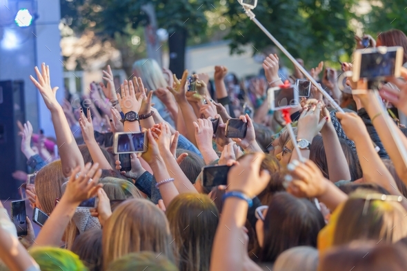 Teenagers at the concert, hands up, using mobile devices, crowd ...