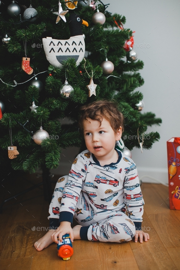 A little boy in pajamas opens a gift in the Christmas morning Stock ...