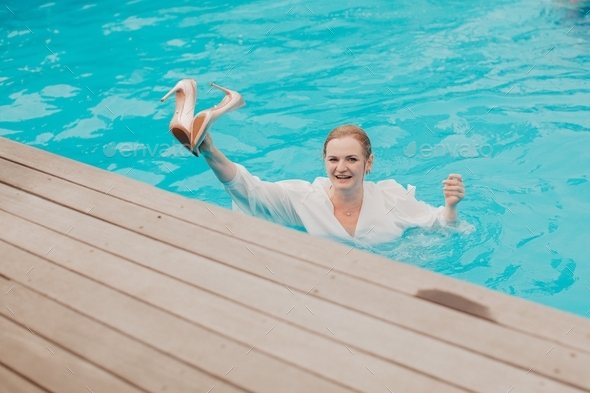 A young beautifully dressed woman in a white dress jumped in the pool ...