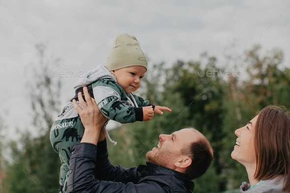 A family with a little boy walks outside, dad throws him into the air ...
