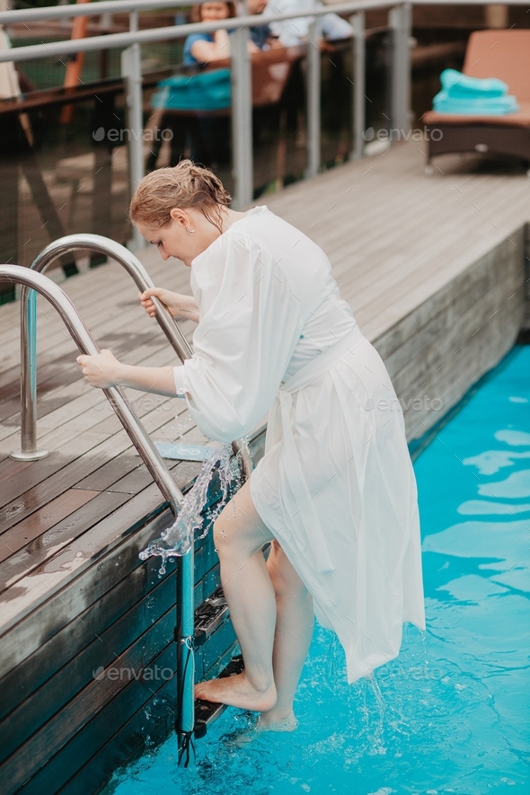 A young beautifully dressed woman in a white dress jumped in the pool ...