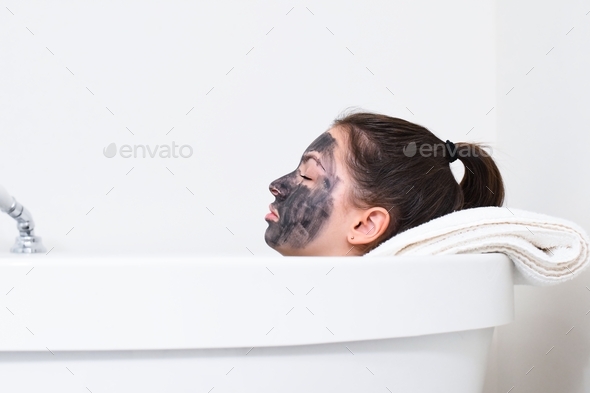 Young teenage girl relaxing with a facial mask laying in a bathtub ...