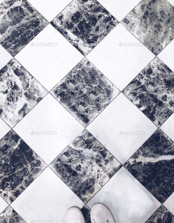 Black and white checkered marble floor with two visible human feet ...