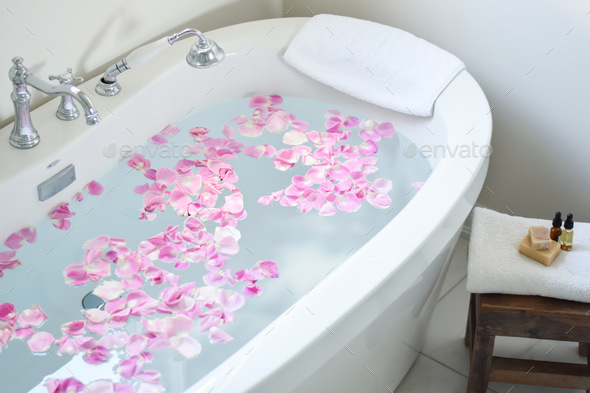 Modern white freestanding bathtub filled with water and pink rose ...