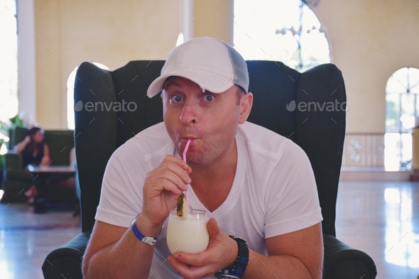 man making silly face while drinking Pina Colada cocktail with pink ...