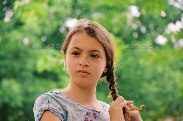 A portrait of a young girl in deep thought, reminiscing while braiding ...
