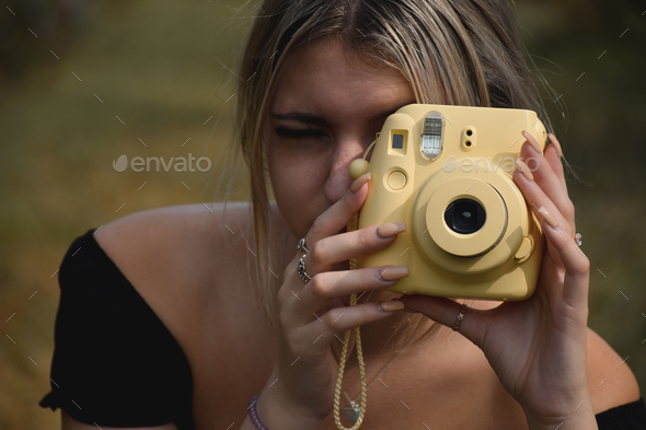 Young teenage girl taking photos with a yellow instant camera outdoors ...