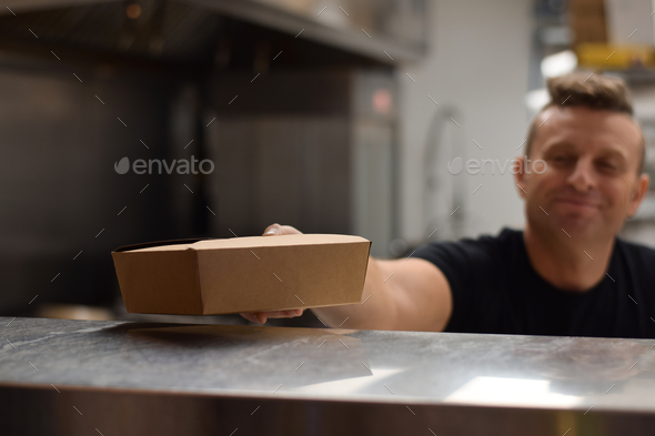 Restaurant kitchen employee is handing a box with take out order ready ...