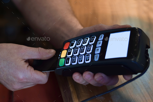 Man’s hand is holding payment machine to make credit or debit payment ...