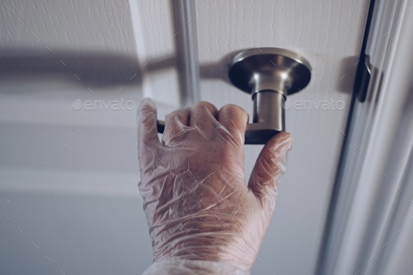 Woman’s hand wearing disposable glove touching a door handle to open ...