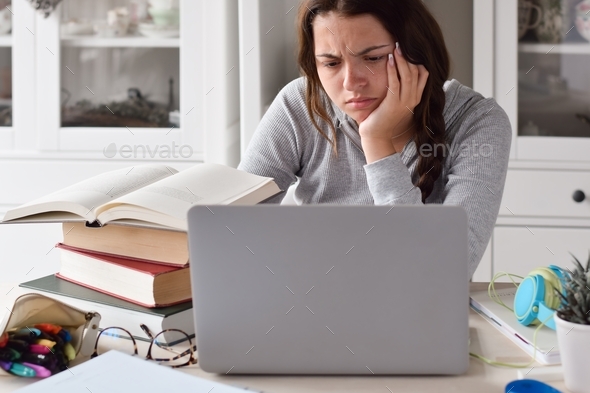 Young teenage girl frowning at something on laptop computer screen ...
