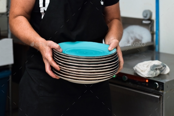 Restaurant kitchen employee carrying stack of clean dishes Stock Photo ...
