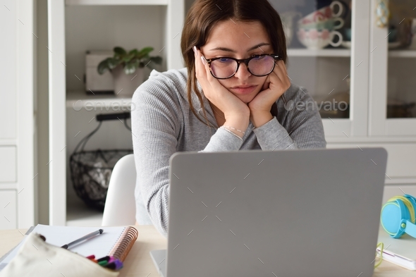 Young teenage girl sitting bored while studying in front of laptop ...