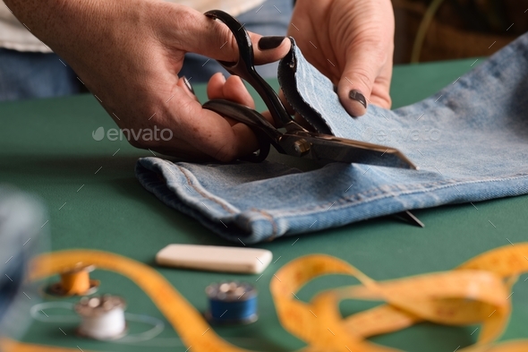 Seamstress cutting length of jeans pants to be hemmed with scissors ...