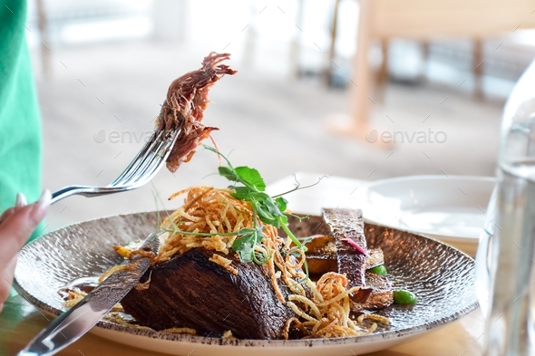 Girl eating short rib dish at a restaurant Stock Photo by JulieAlexK