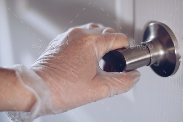 Woman’s hand wearing disposable glove touching a door handle to open ...