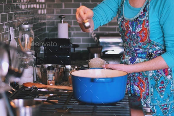 Woman is adding salt while cooking dinner in a blue cast iron pot ...