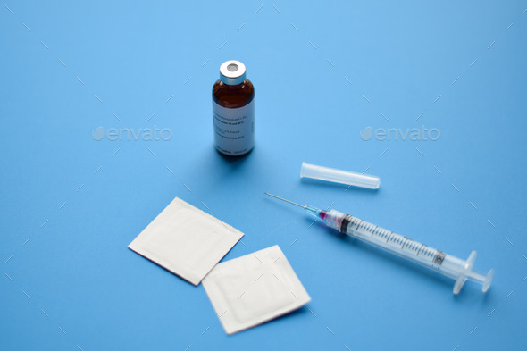 Syringe, a medication vial and alcohol wipes for an injection on blue ...