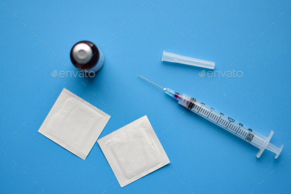 Syringe, a medication vial and alcohol wipes for an injection on blue ...