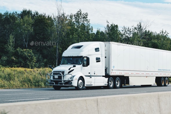 All white tractor trailer driving on a highway transporting and ...